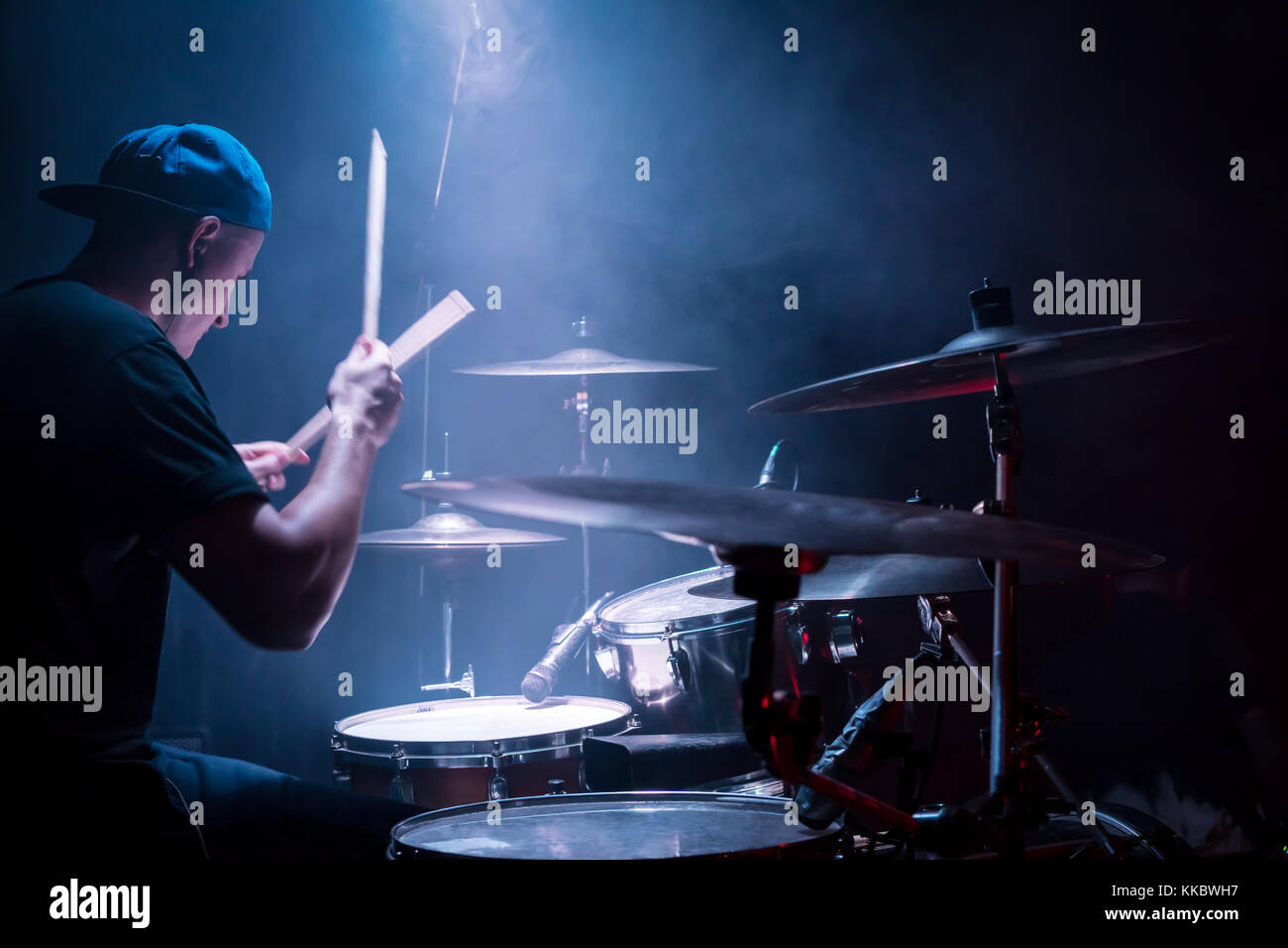 Drummer in a cap and headphones plays drums at a concert under blue ...
