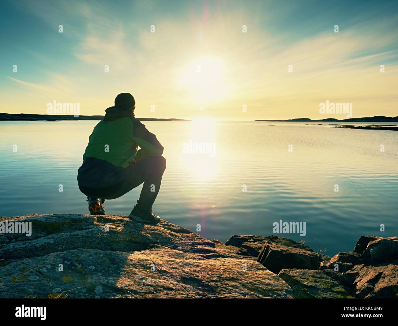 Tired man sit on rocky sea coast. Calm water, rocky island and sunset ...