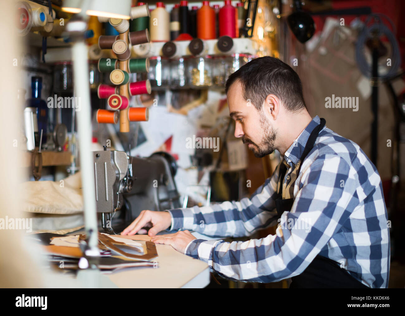 Smiling american male worker sewing stitches on belt in leather ...