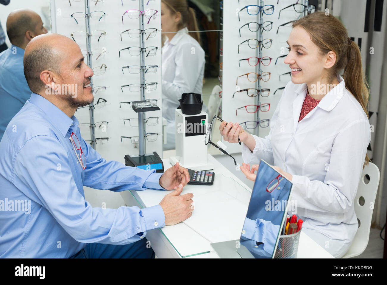 Professional young female optician helping senior client to choose a ...