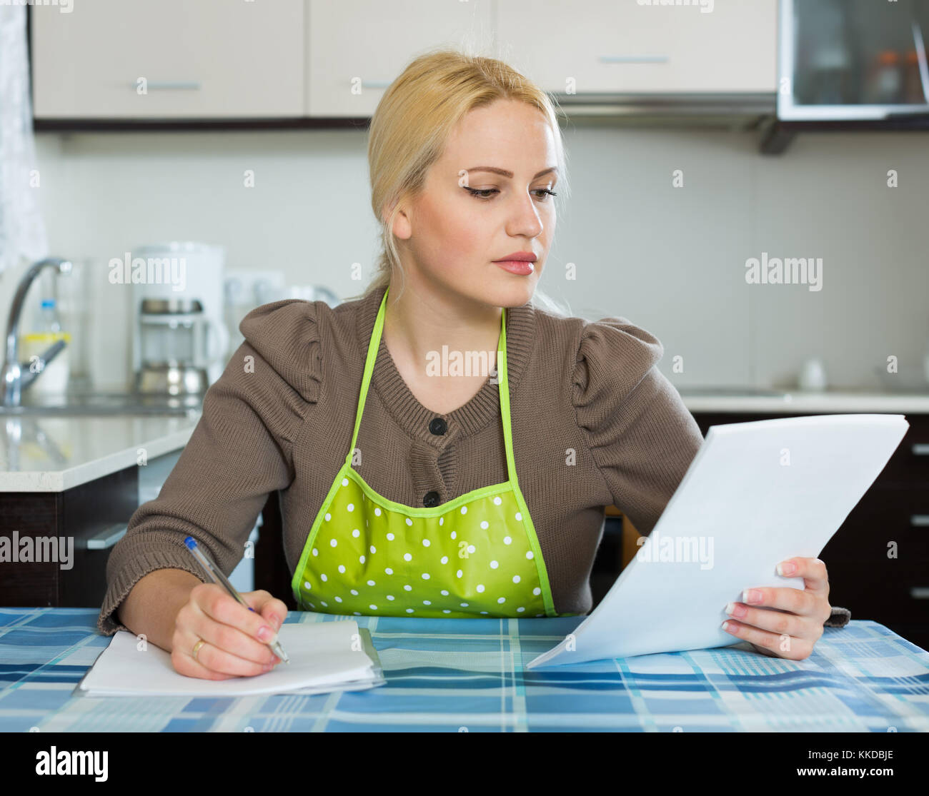 Serious woman filling in the financial documents at table in home ...