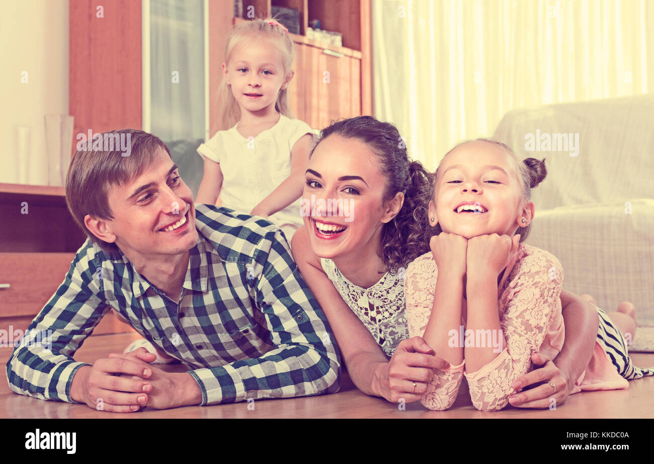Portrait of cheerful parents with two daughters laying on the floor at ...