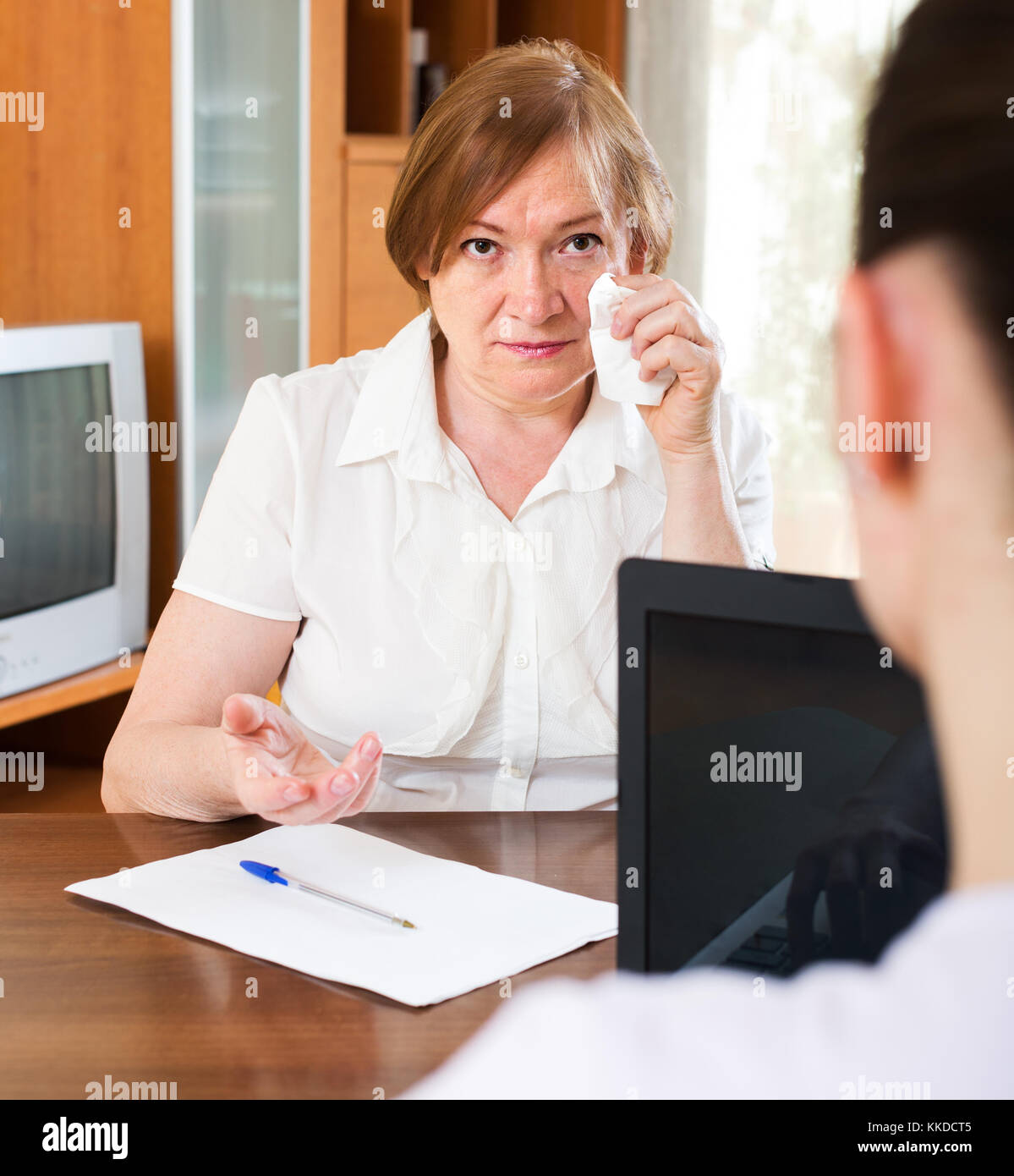 Sad woman talking with worker at table in interior of home or office ...