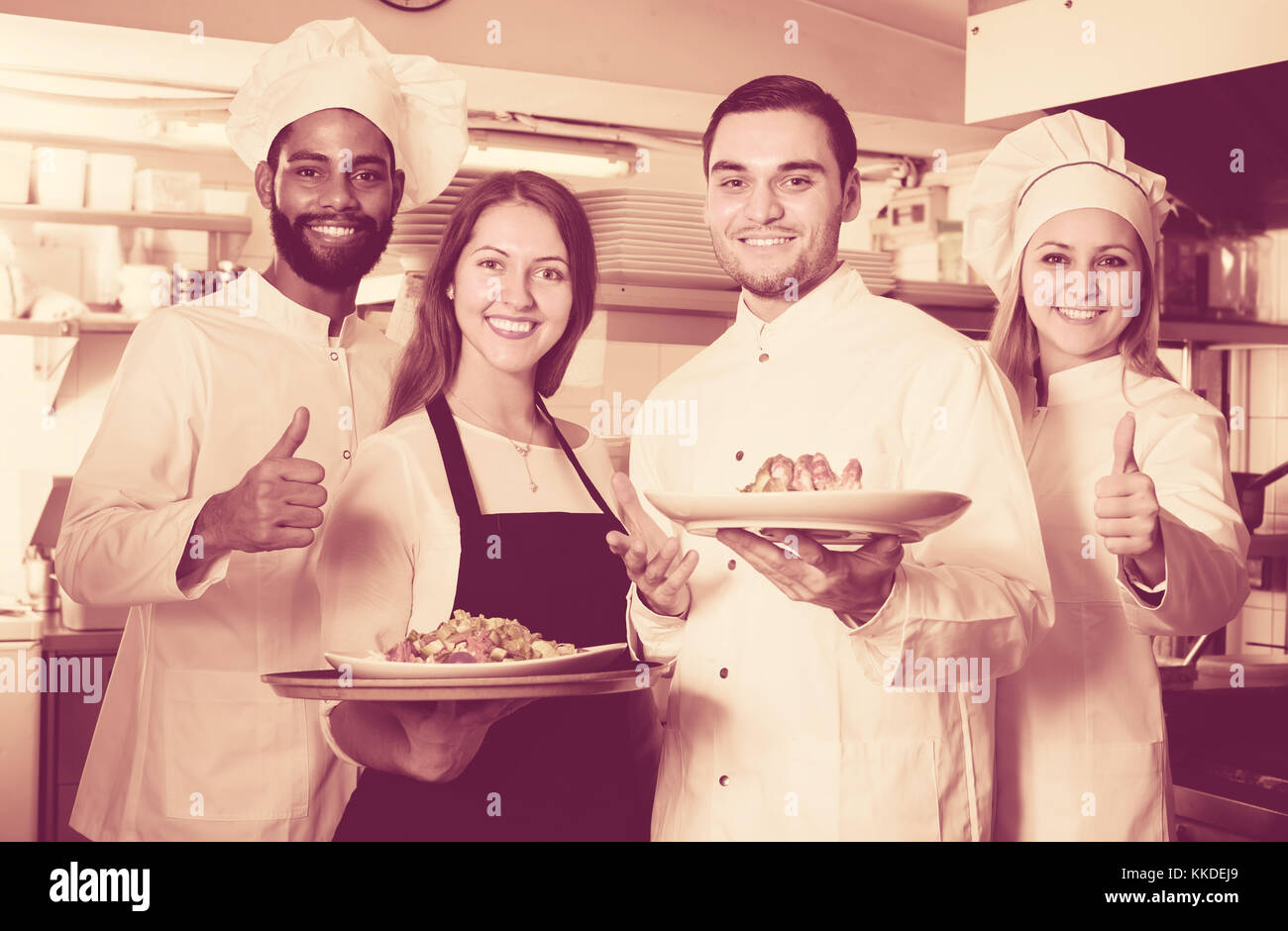 happy waitress and crew of professional cooks posing at restaurant ...
