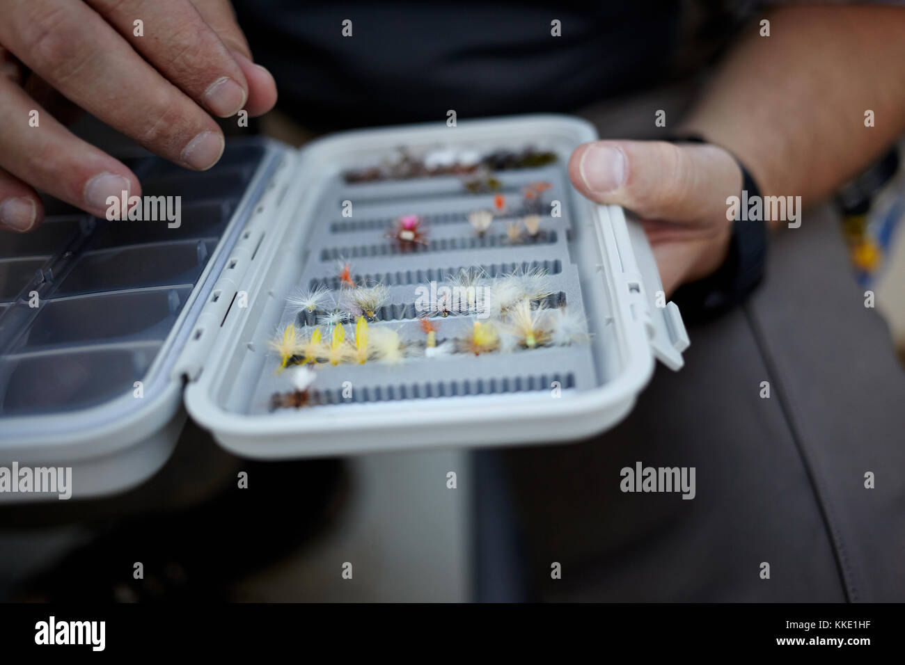 Fly fisherman selecting a specific fly from a plastic box containing ...