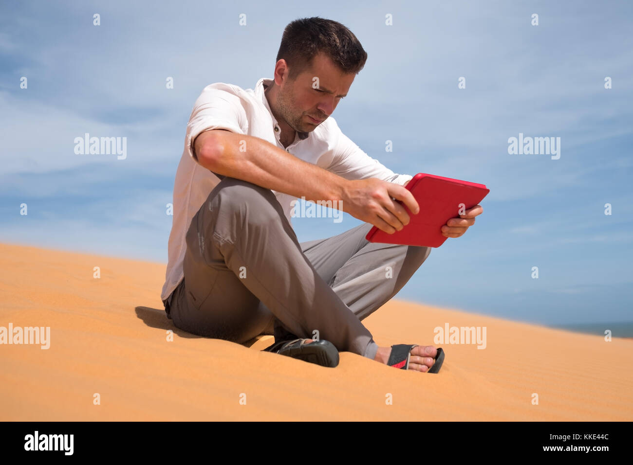 Lost in the desert. Caucasian man sitting on sand with tablet. He is ...