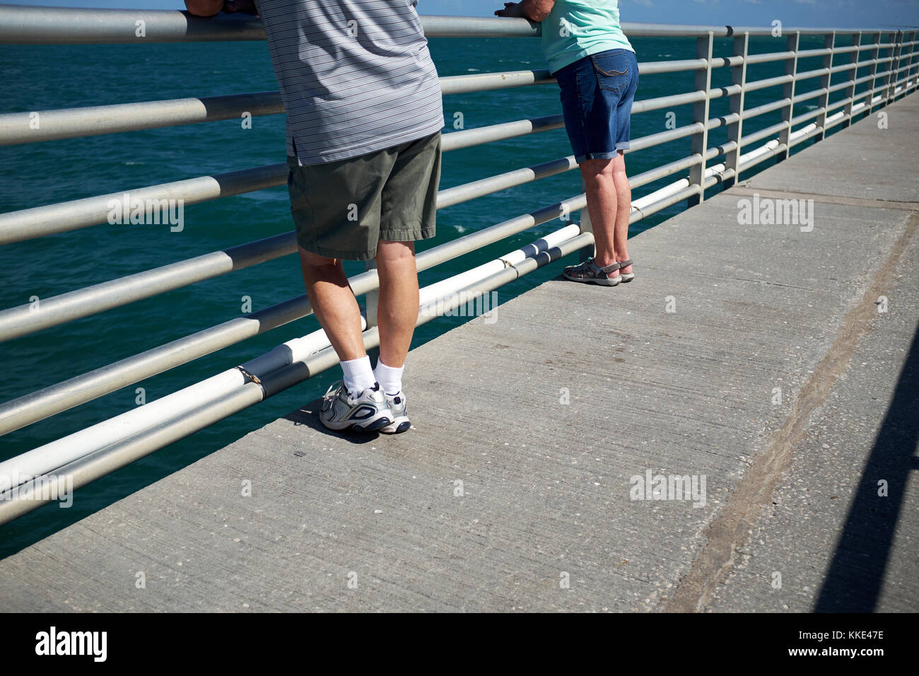 Two people standing on a promenade leaning on the metal rails ...