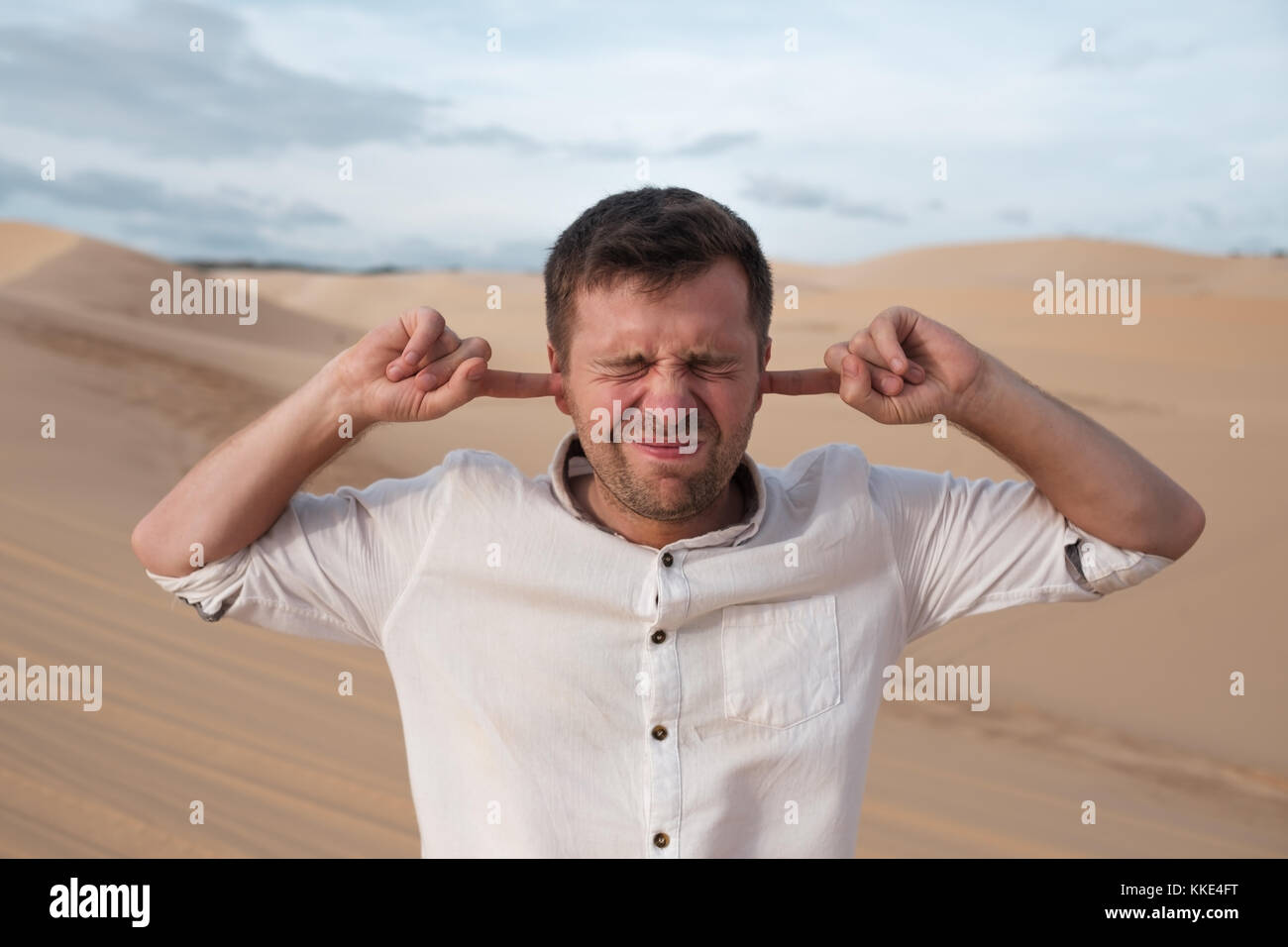 A middle-aged man stands alone in desert and closes his ears with his ... A middle-aged man stands alone in desert and closes his ears with his ...