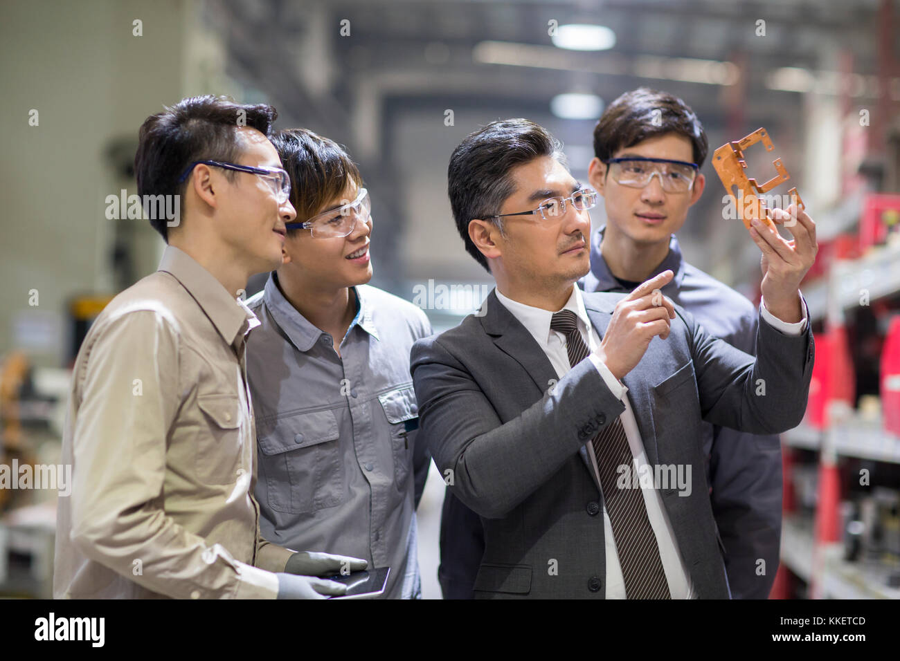 Chinese businessman and engineers checking machine parts in the factory ...