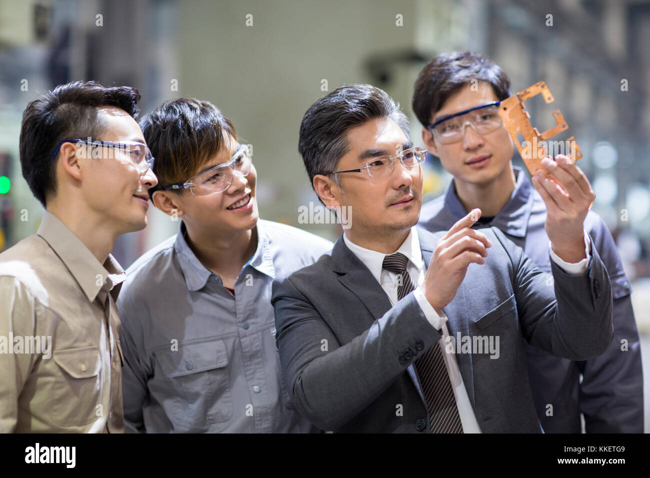 Chinese businessman and engineers checking machine parts in the factory ...