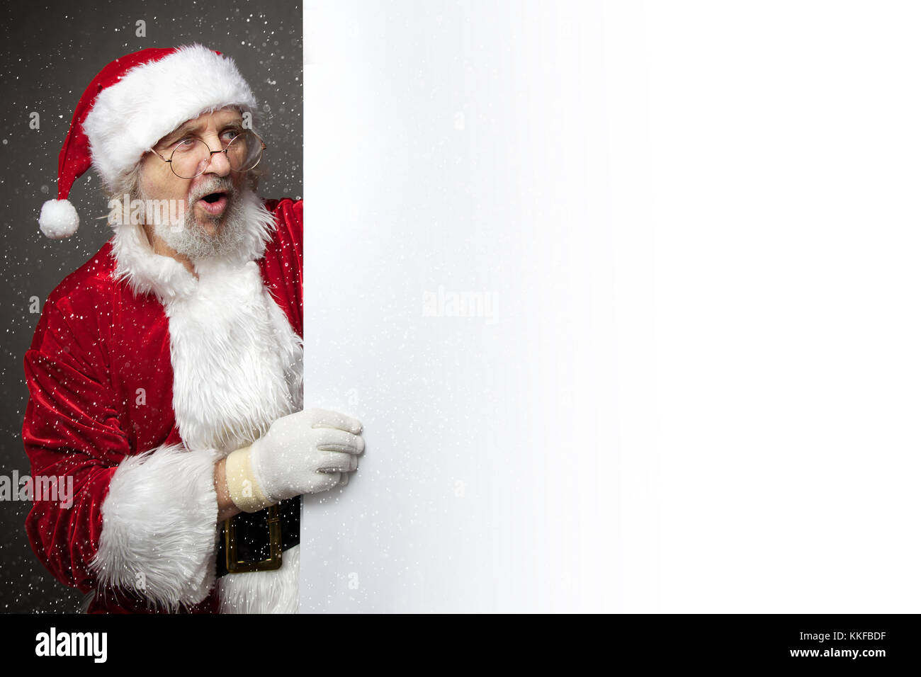 Surprised Santa Claus showing something on a white wall Stock Photo - Alamy