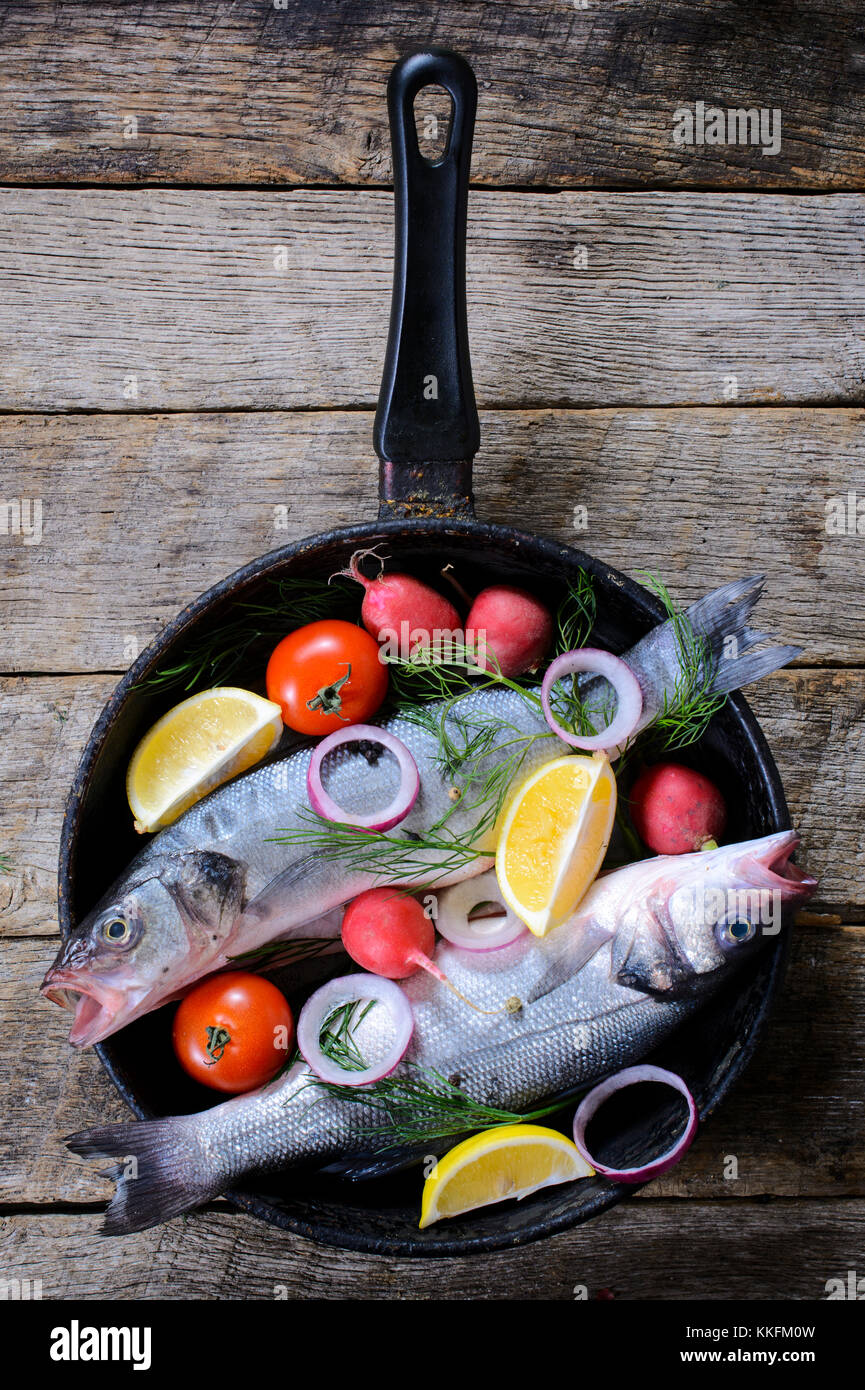 Bass fish and vegetables in the pan on wooden background from above ...