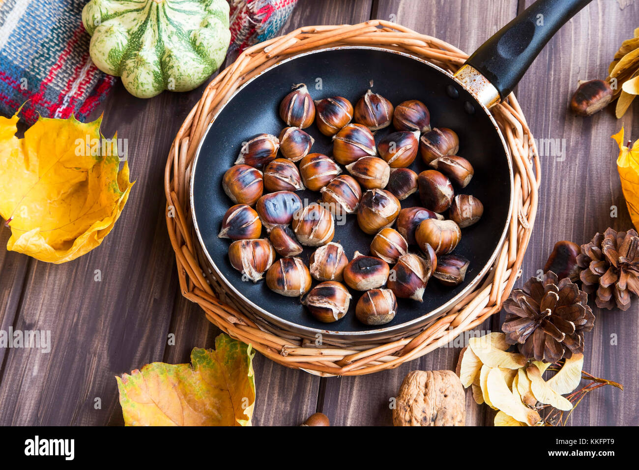 Roasted chestnuts in a pan top view with autumn dried leaves , cones ...