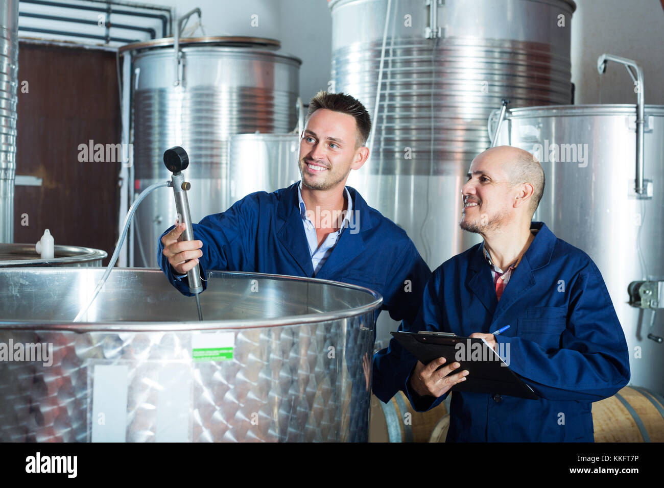 Adult positive winery workers taking notes while checking equipment in ...