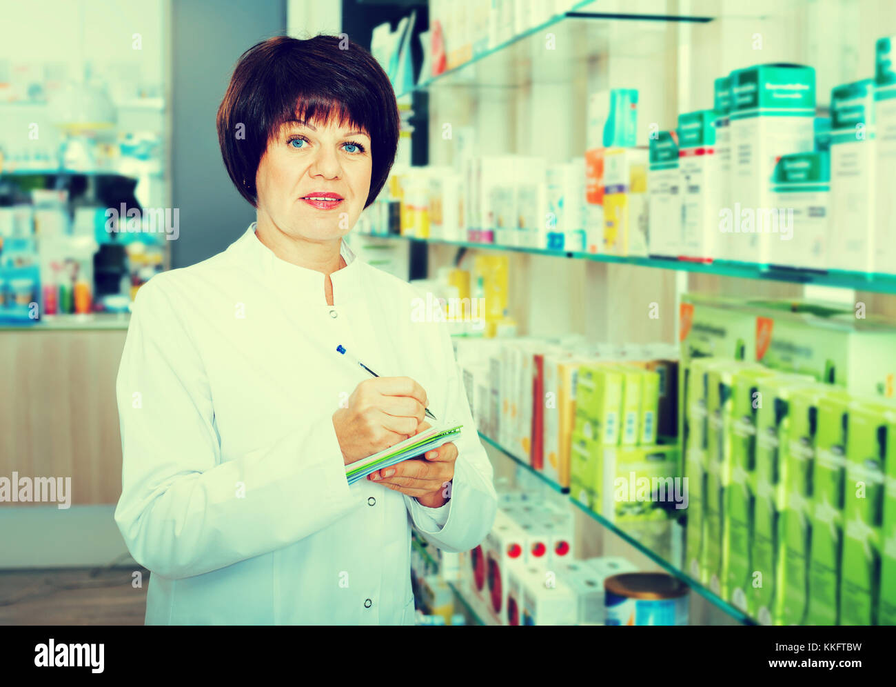 Positive woman druggist wearing white coat standing among shelves in ...