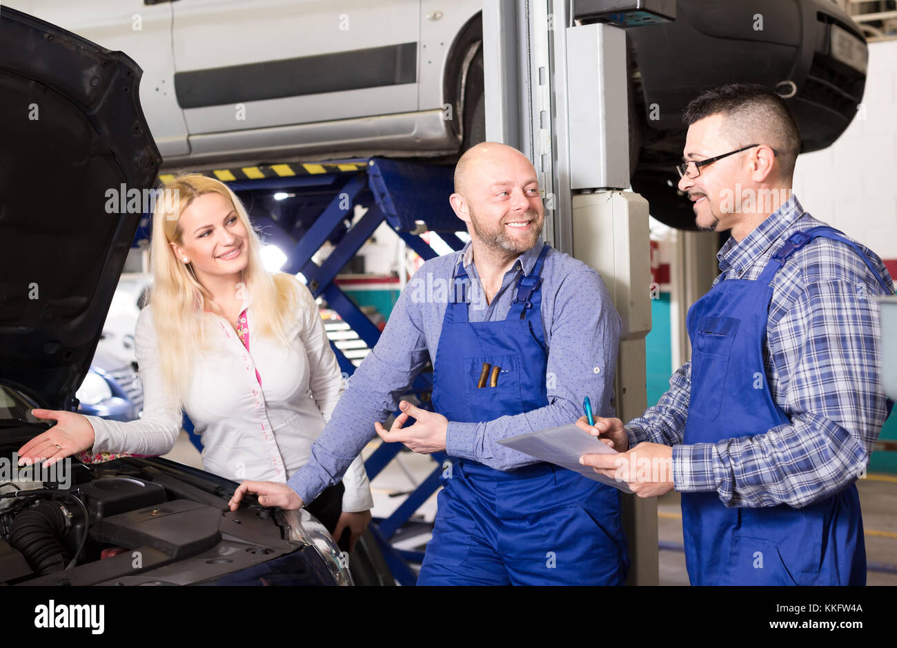 Two happy mechanics and a female driver examine a car at a repair shop ...