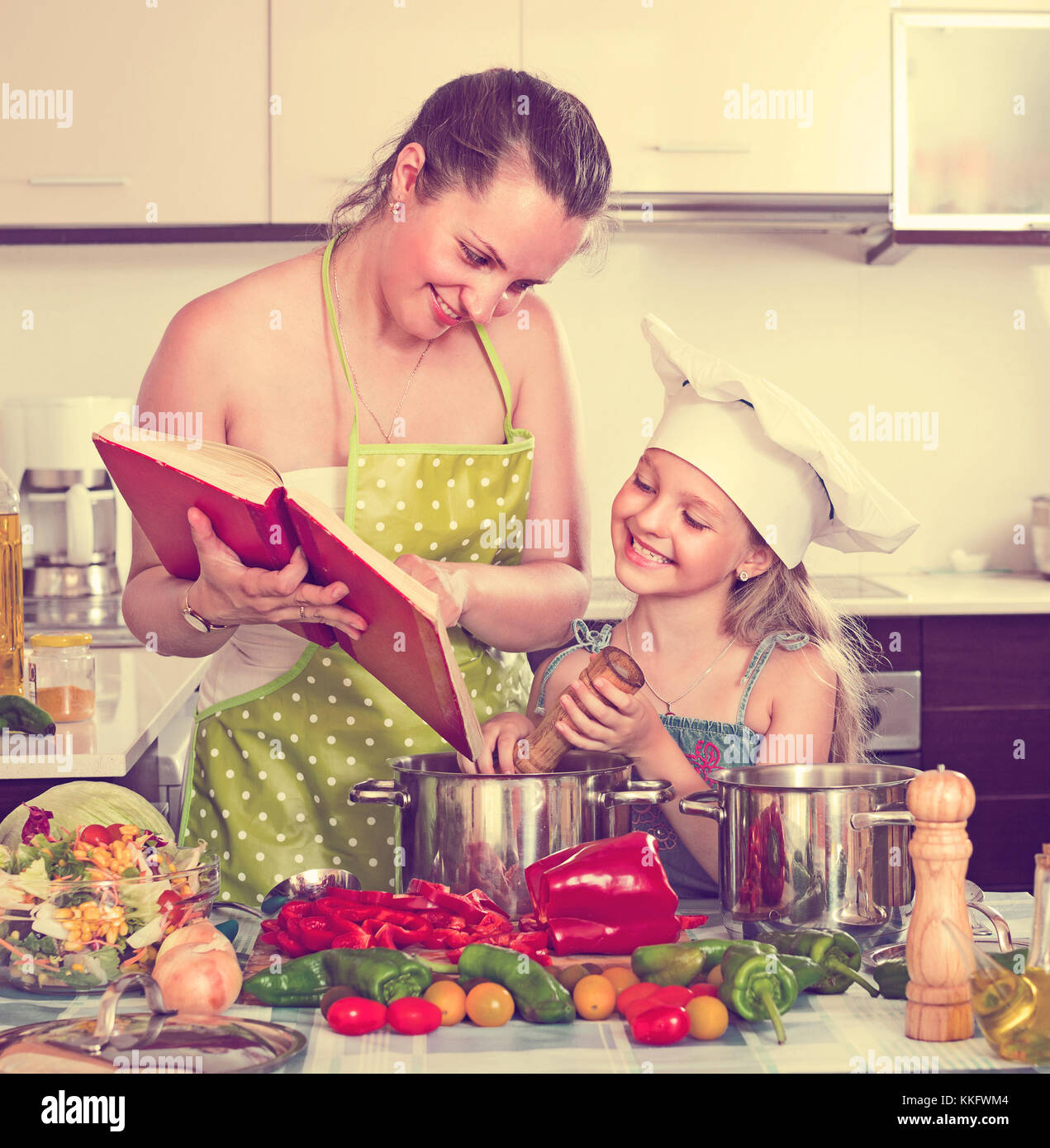 Smiling little girl with mom learning new recipe from cookery book at ...