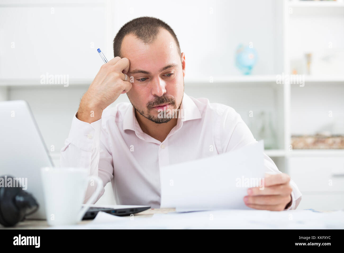 Confused young married man reading documents at his workplace near ...