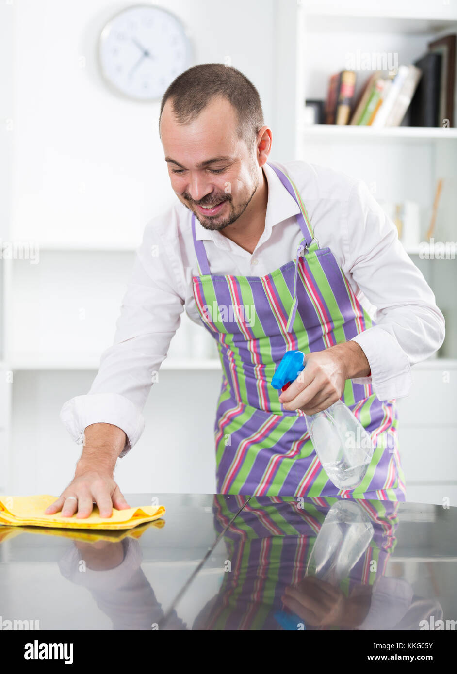 Positive young man in apron cleaning his office desk by cleanser Stock ...