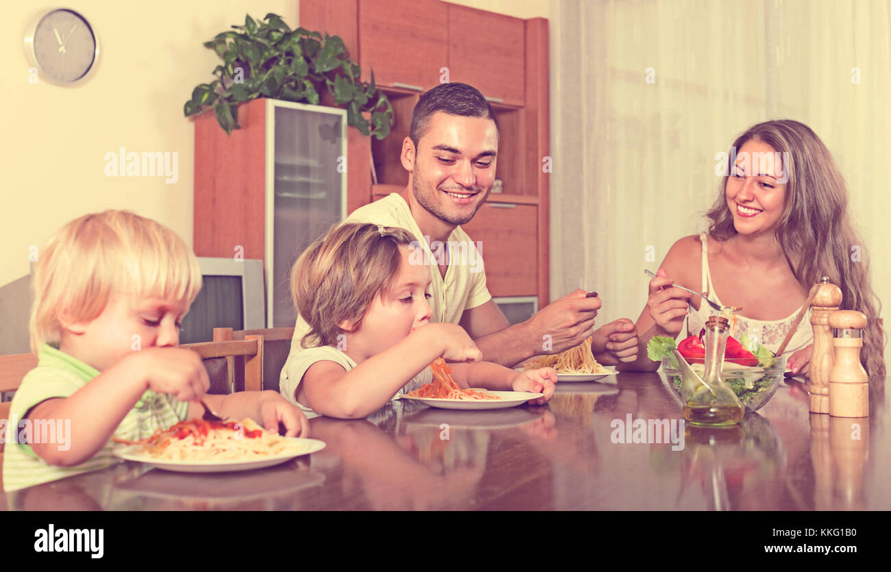 Young smiling family of four eating spaghetti at home interior. Focus ...