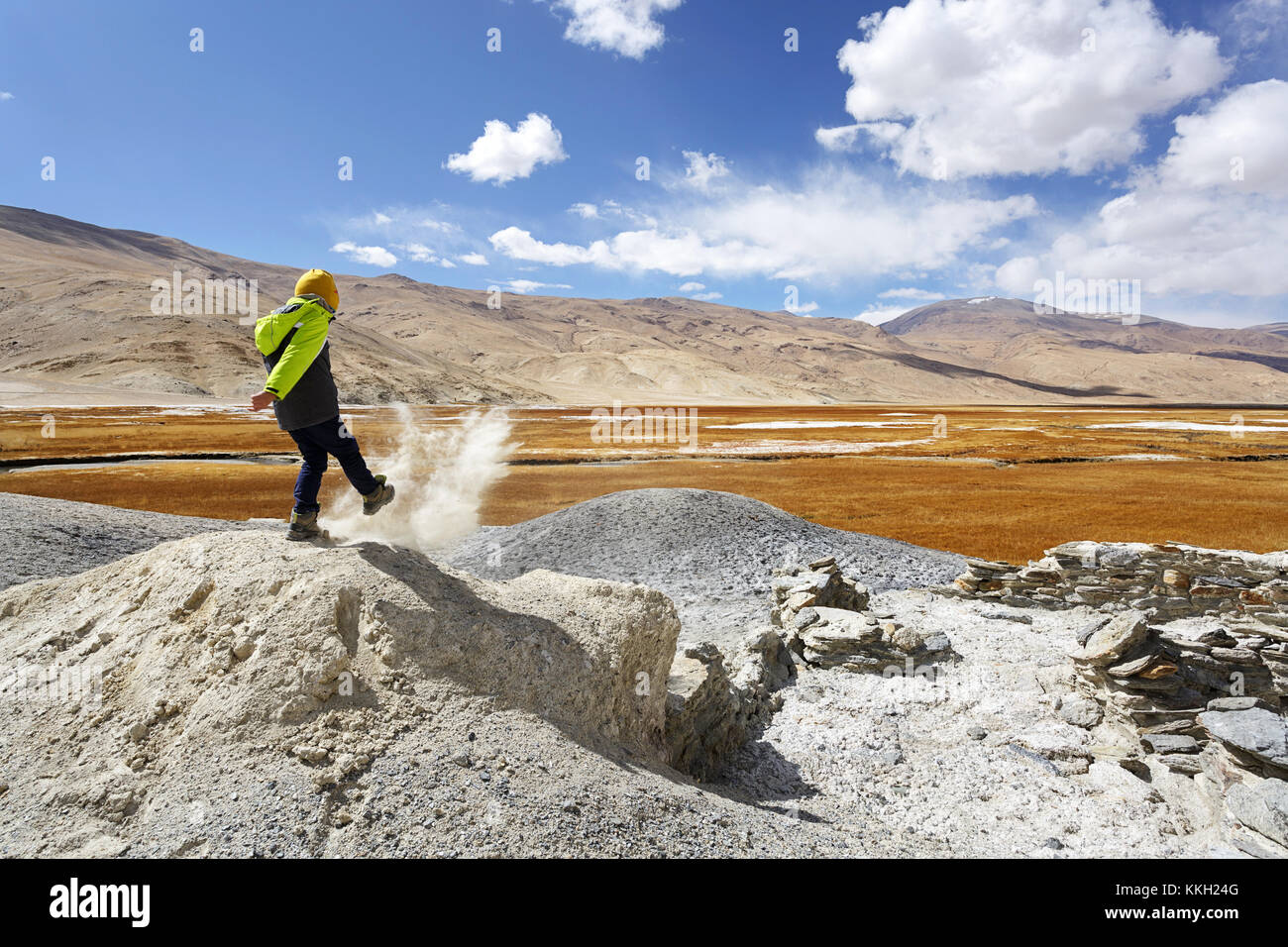 Young caucasian boy standing on the rock and kicking the white dust in ...