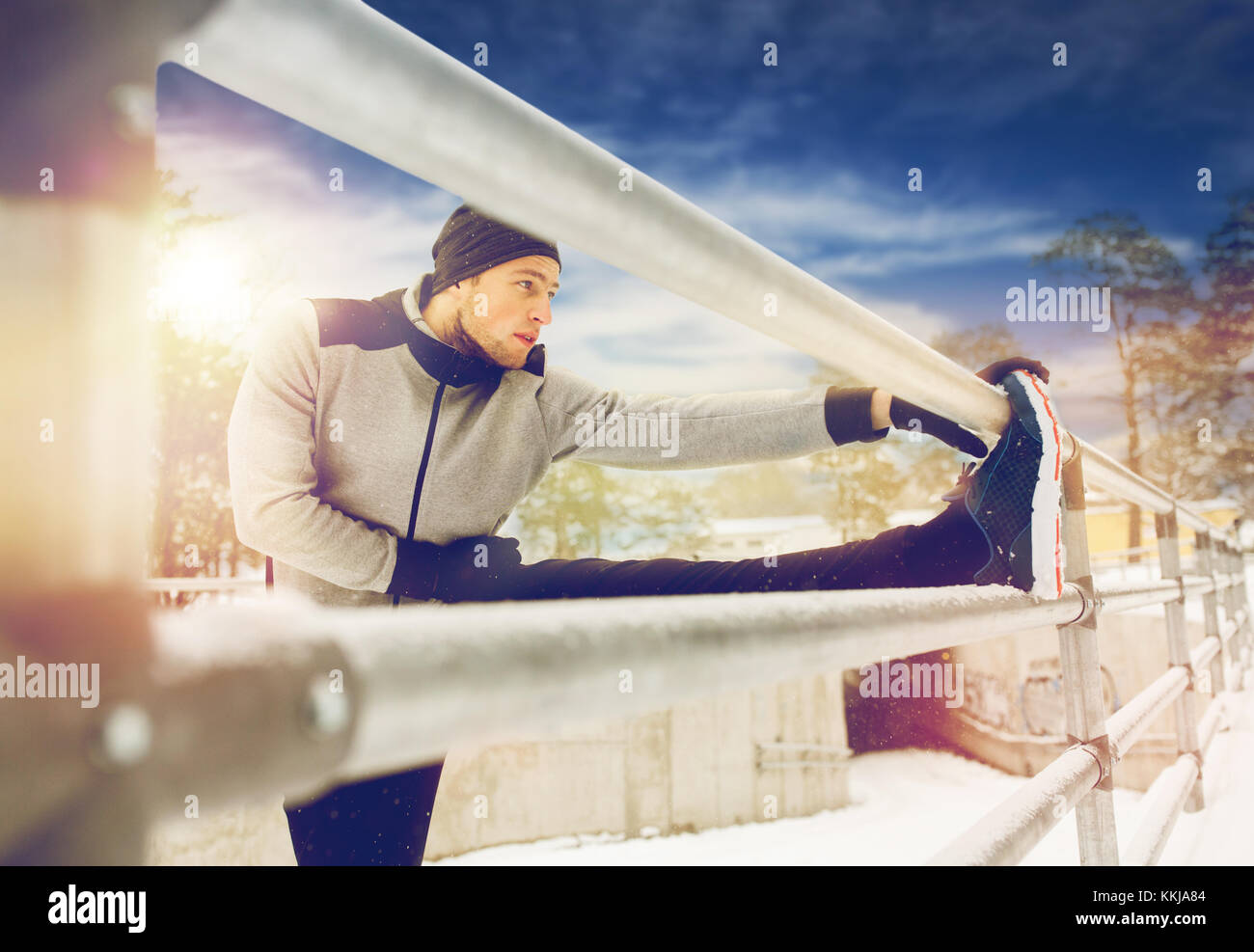 sports man stretching leg at fence in winter Stock Photo - Alamy