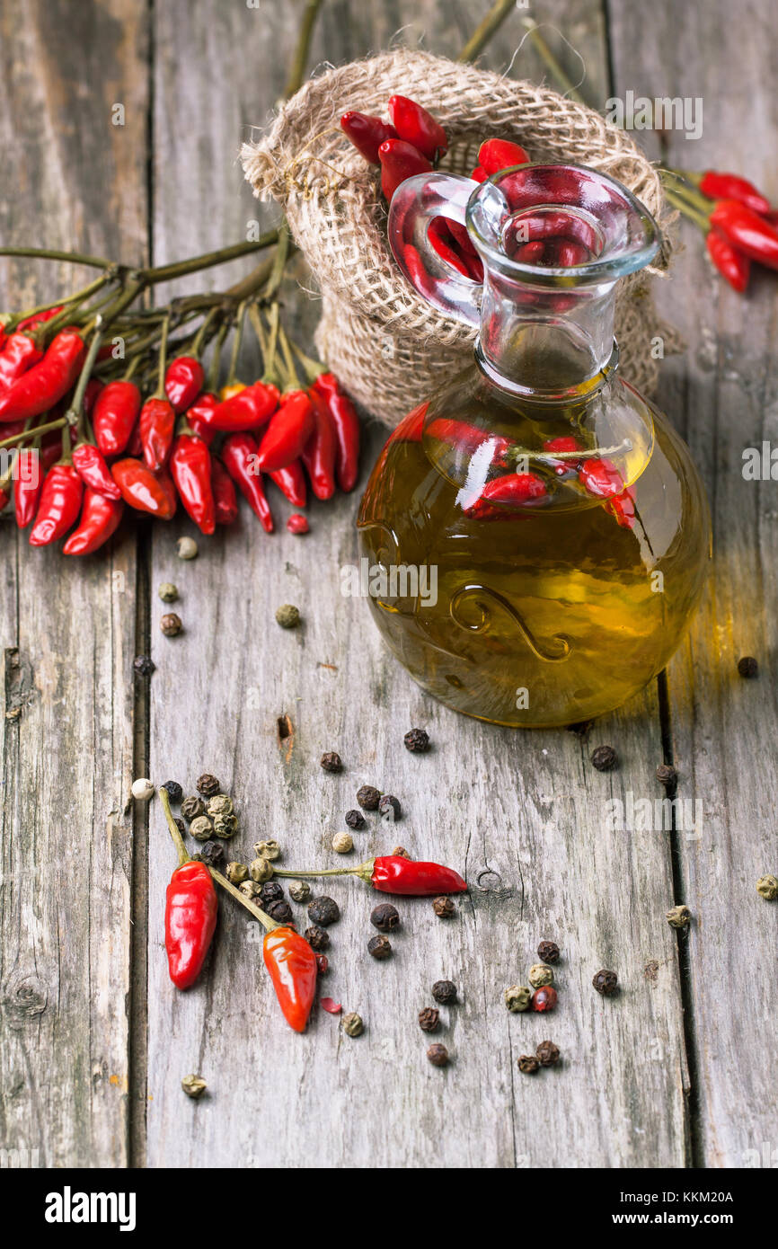 Glass bottle of olive oil with red hot chili peppers over old wooden ...