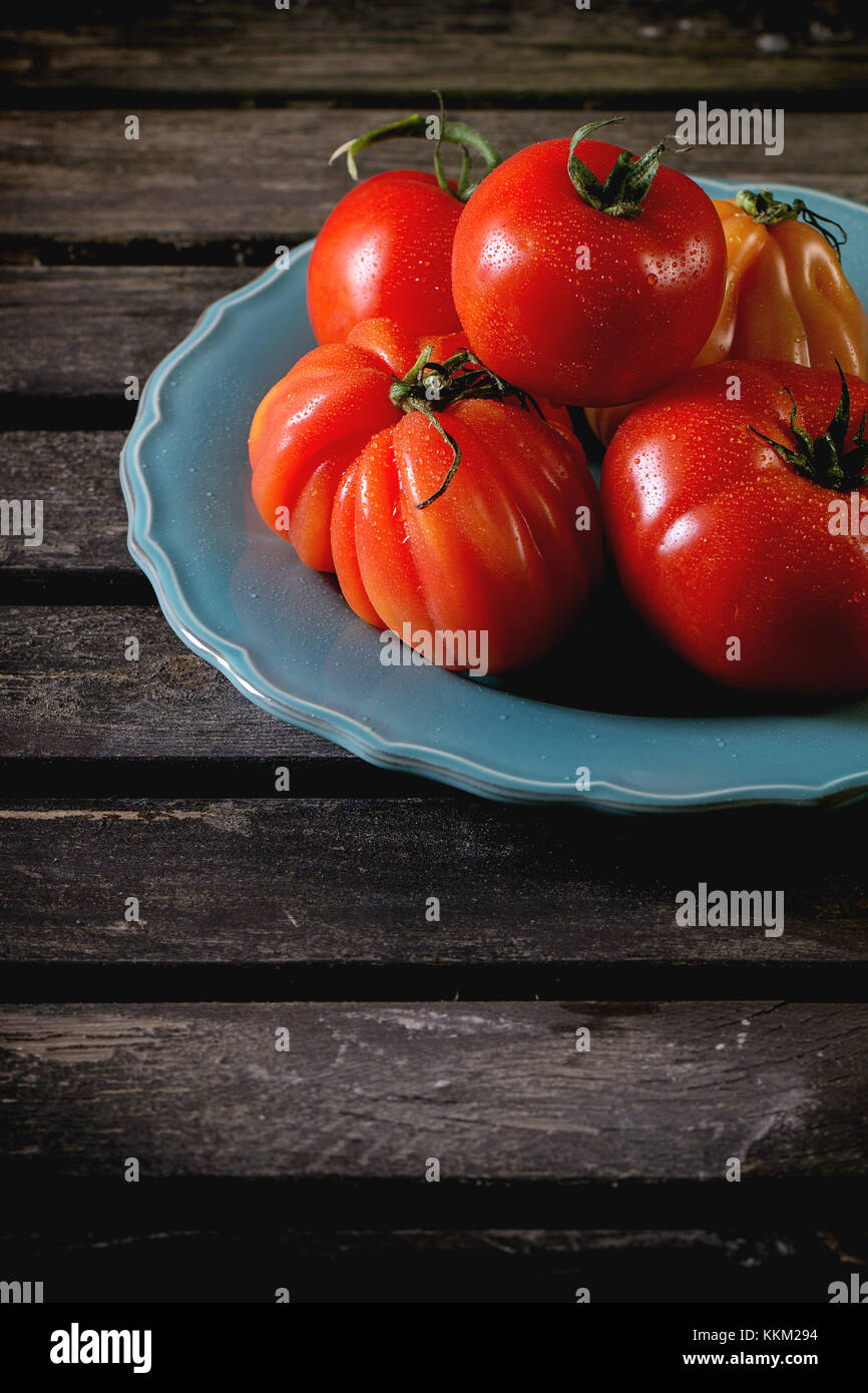 Heap of big red tomatoes RAF on turquoise plate over old wooden table ...