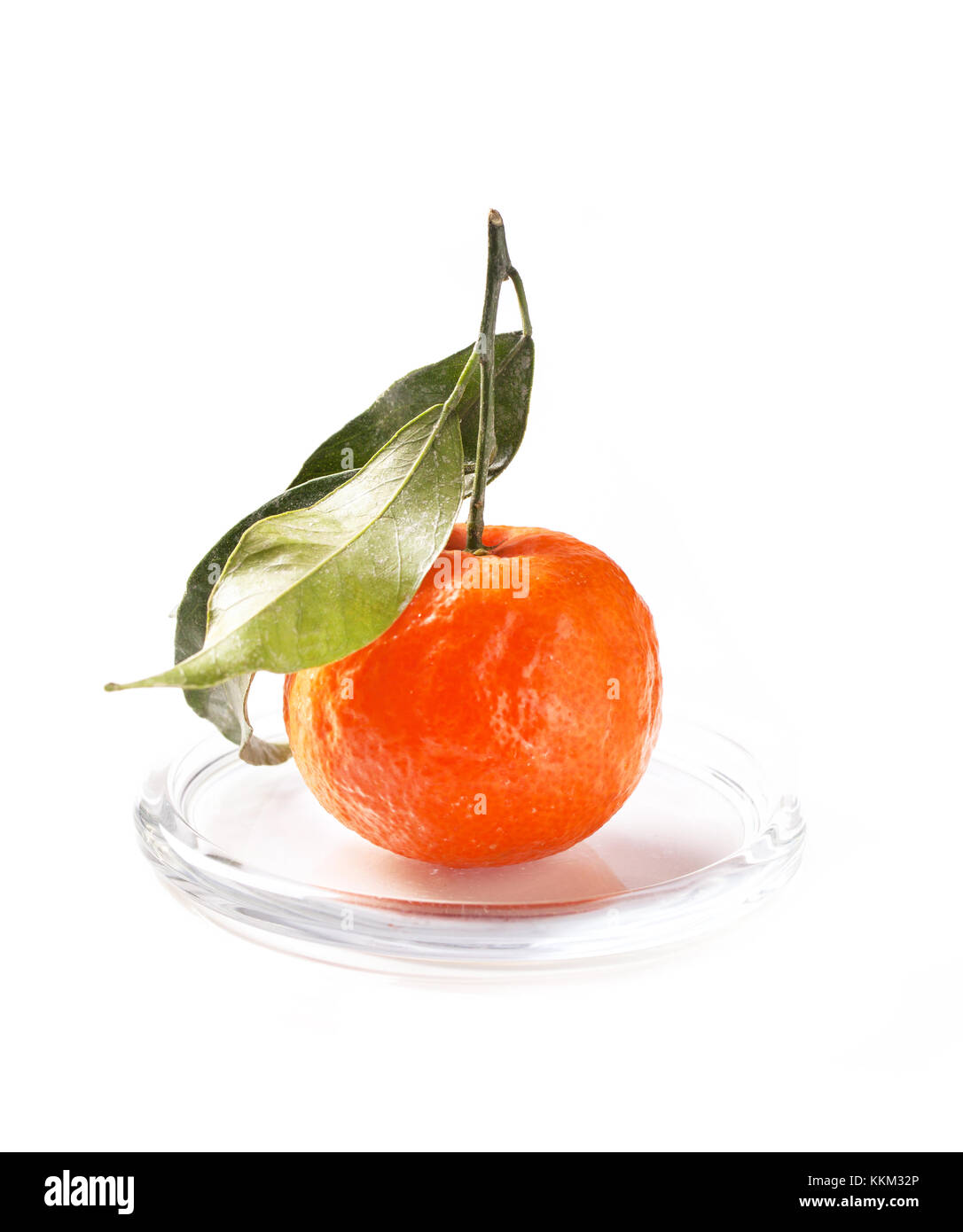 One tangerine with leaves on glass saucer isolated over white Stock ...