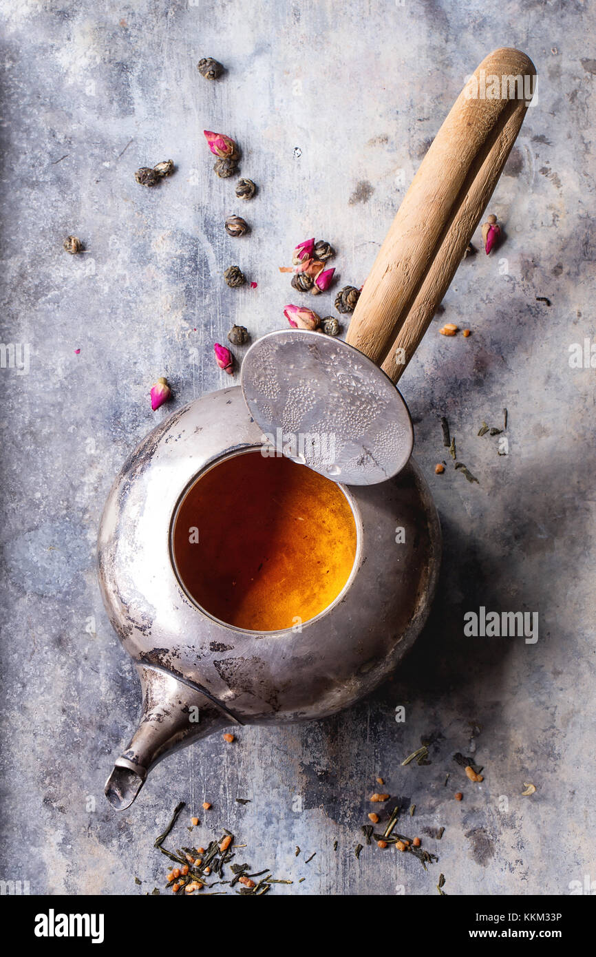 Open vintage metal teapot with wooden handle. With dry green tea leaves ...