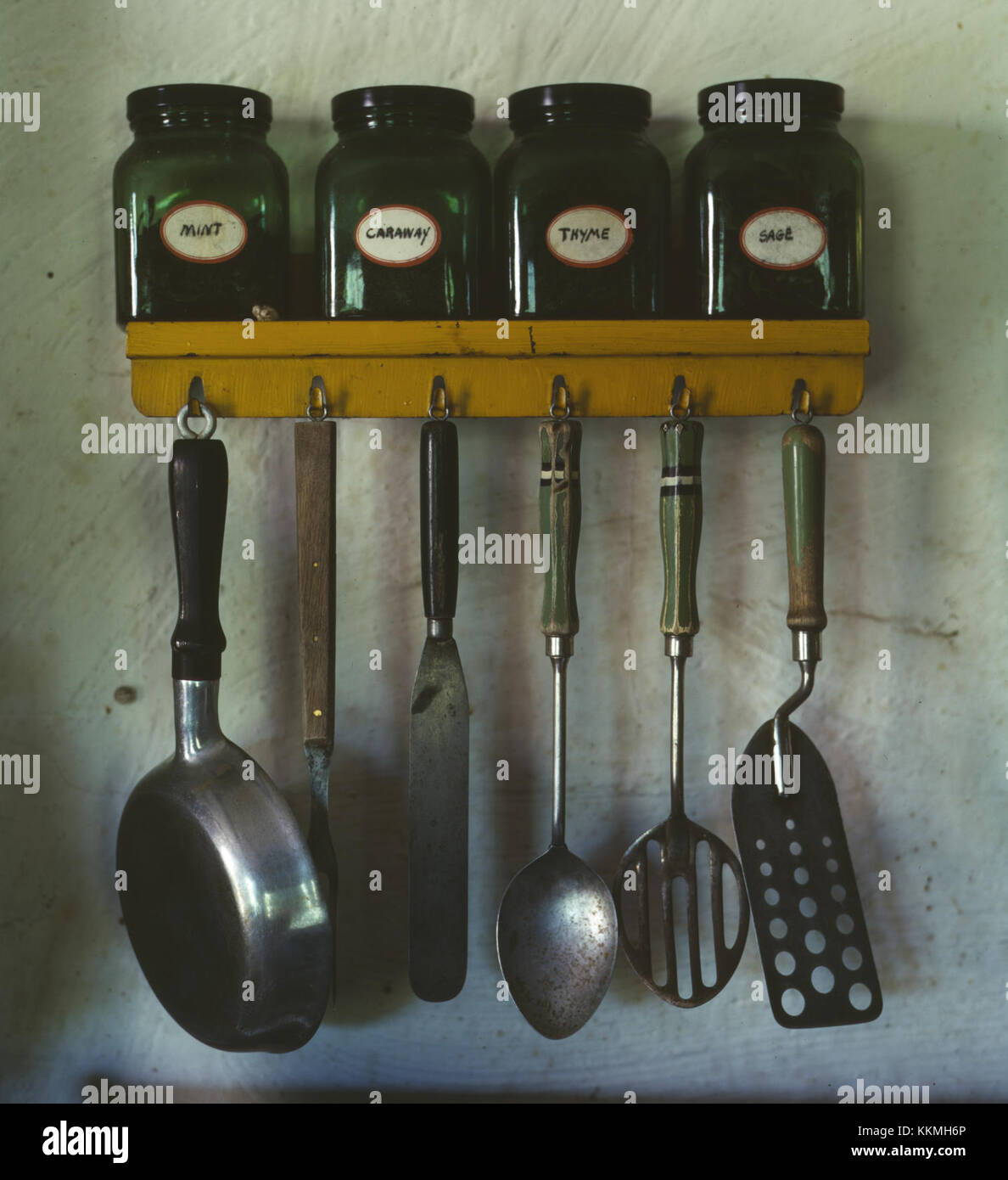 A collection of kitchen utensils is arranged below a spice rack ...