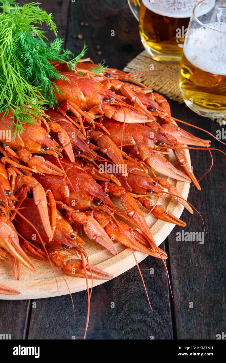 A pile of large crawfish on a wooden tray, glasses with beer on a dark ...