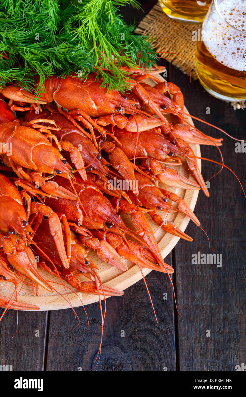 A pile of large crawfish on a wooden tray, glasses with beer on a dark ...
