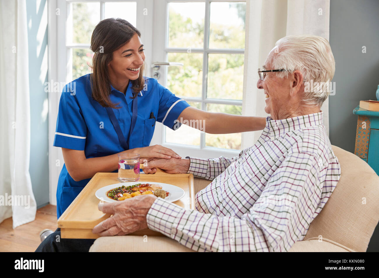 Nurse serving dinner to a senior man in an armchair at home Stock Photo ...