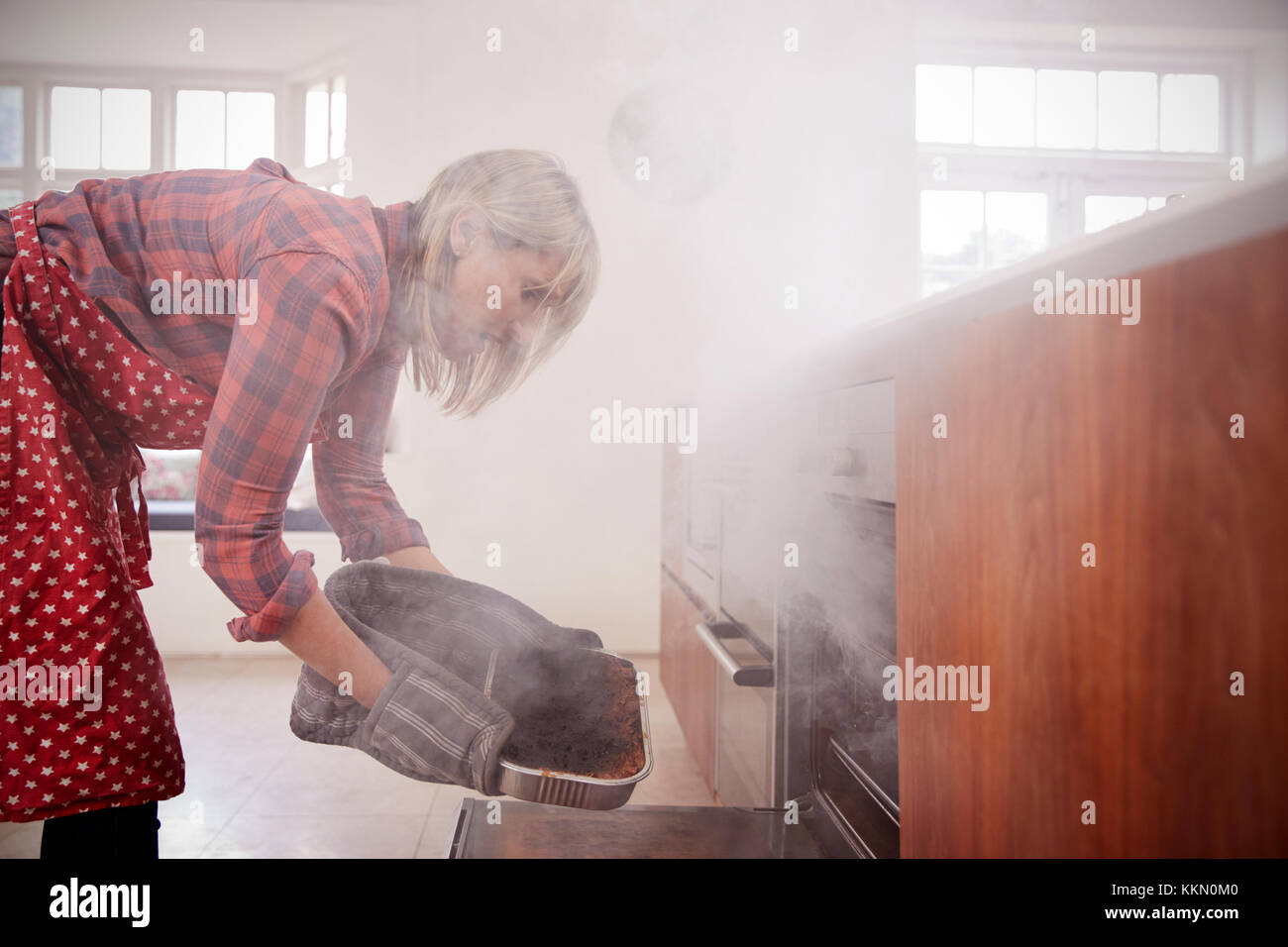 Middle aged woman opening smoke filled oven in the kitchen Stock Photo ...