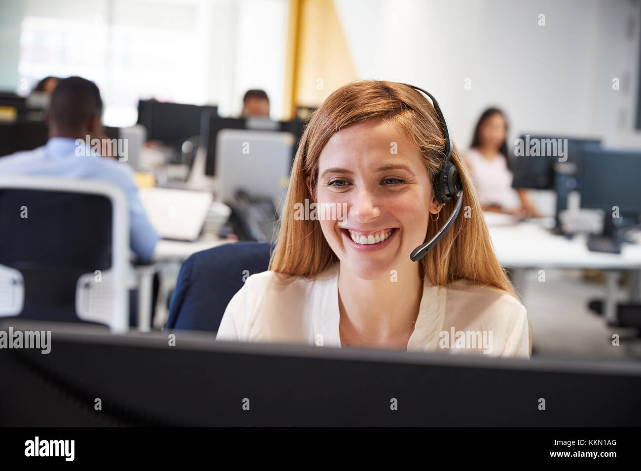 Young woman working at computer with headset in busy office Stock Photo ...