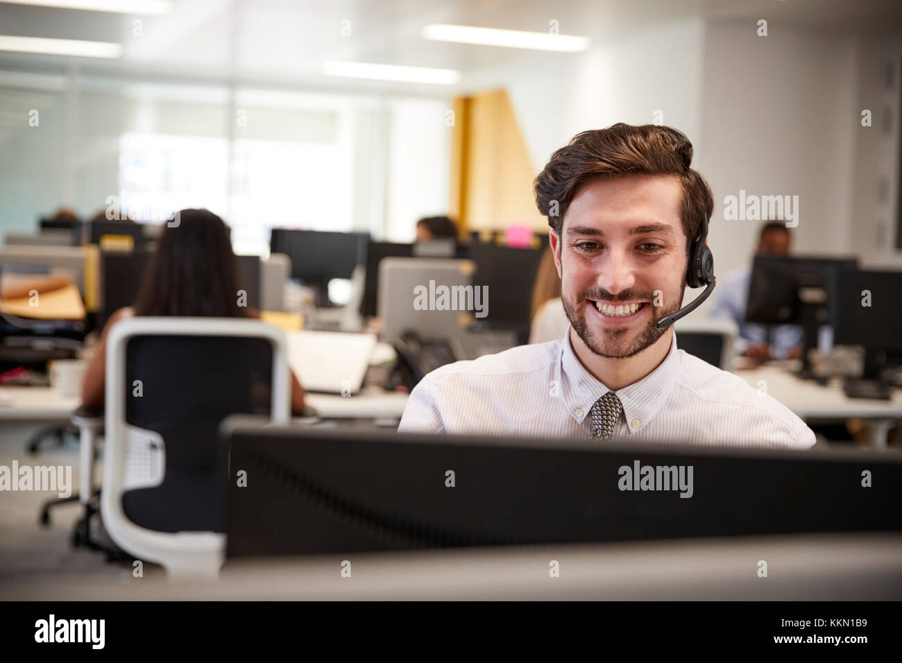 Young man working at computer with headset in busy office Stock Photo ...