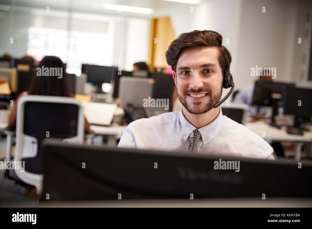 Young man working at computer with headset in busy office Stock Photo ...