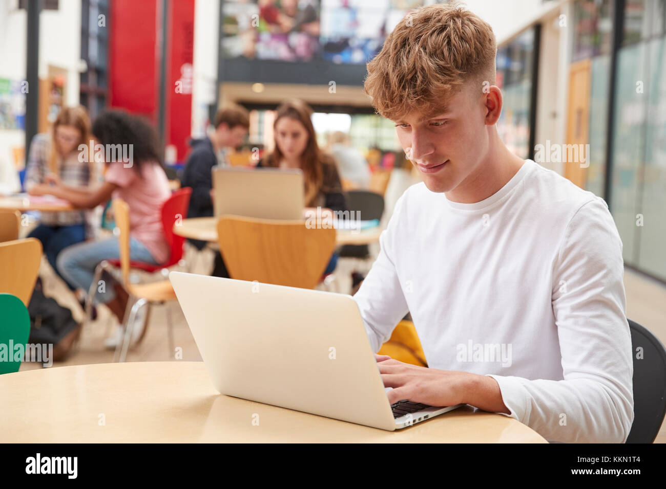 Male Student Working In Communal Area Of Busy College Campus Stock ...