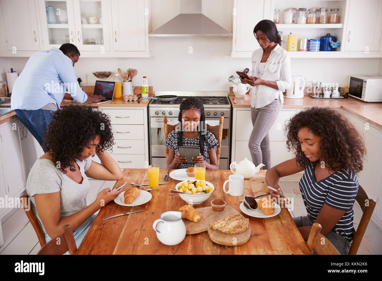 Family Sitting Around Breakfast Table Using Digital Devices Stock Photo ...