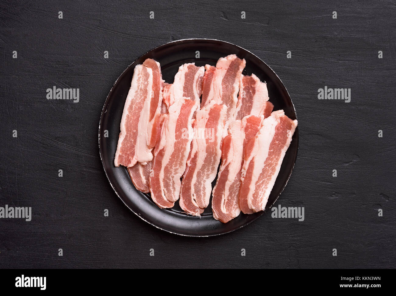 Raw sliced bacon ready for cooking on black stone background. Top view ...