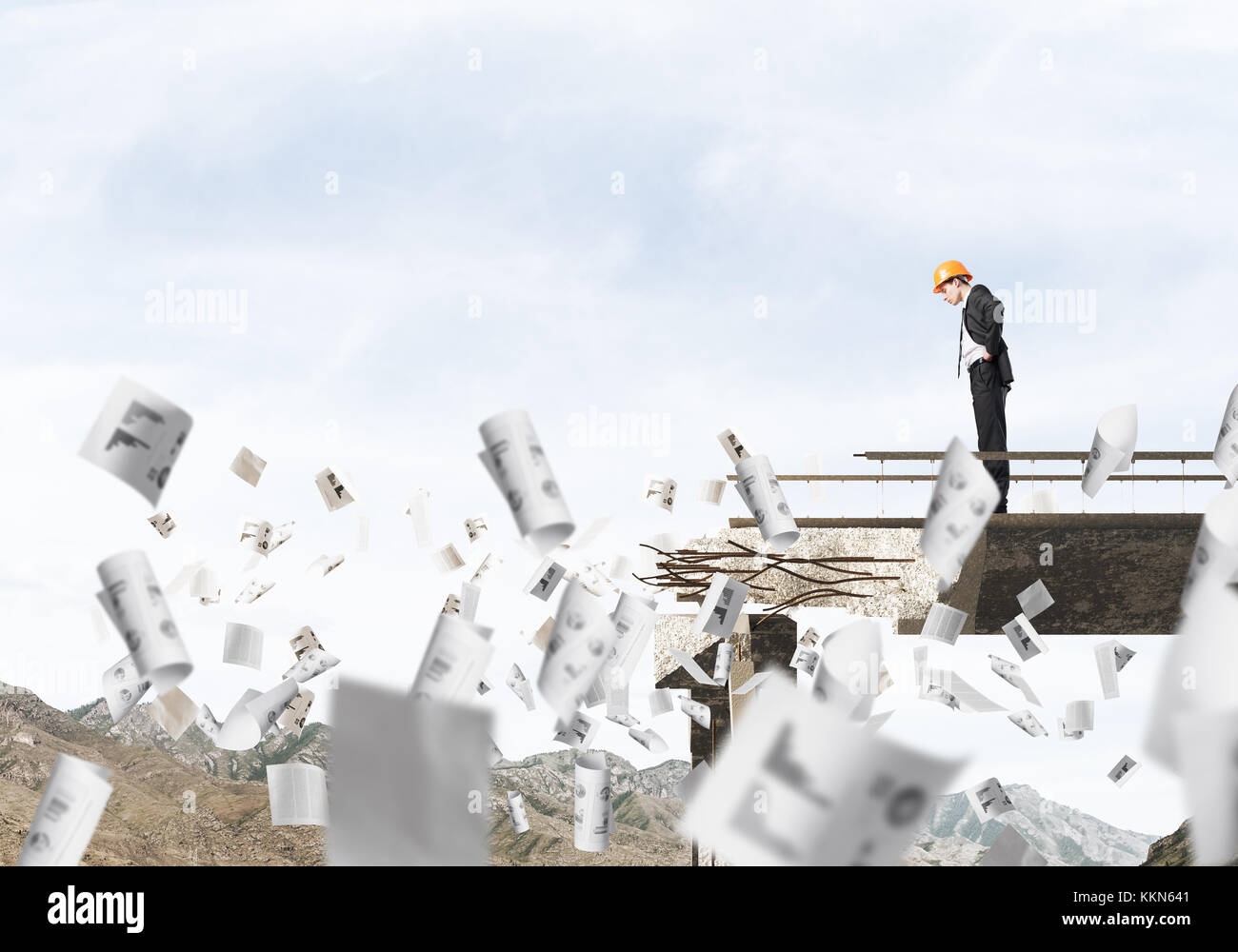 Young engineer in suit and helmet looking down while standing among ...