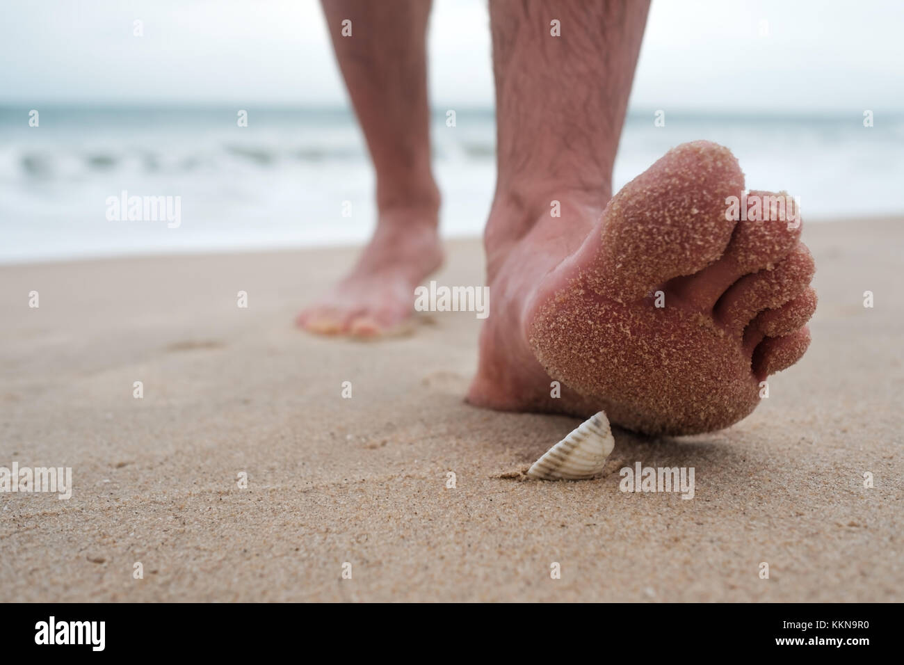 Man goes on the beach and is going to stand up on broken sharp shell ...