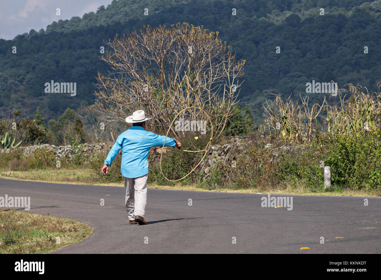 A Mexican cowboy walks down a rural road practicing his lasso skills ...