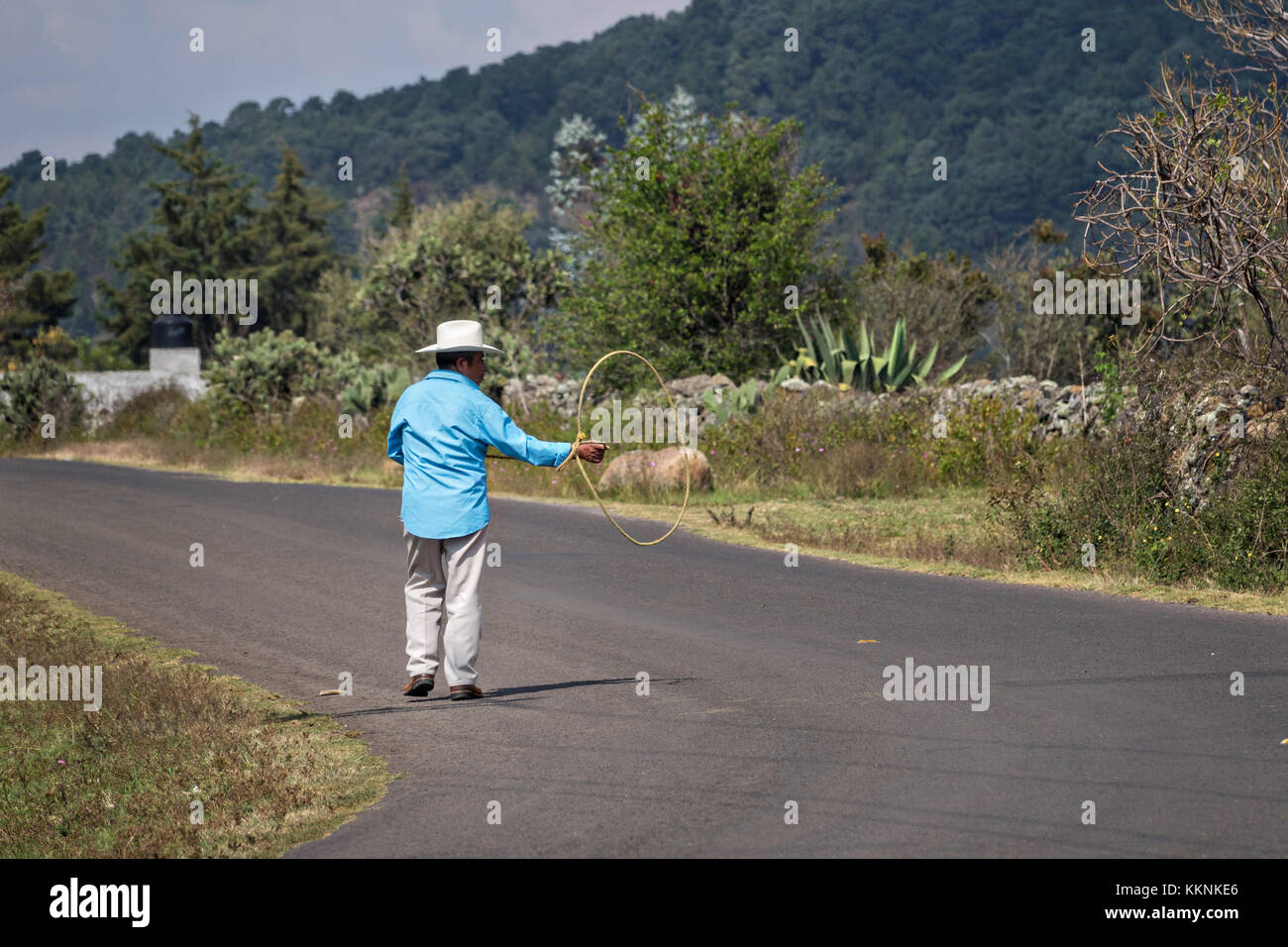 A Mexican cowboy walks down a rural road practicing his lasso skills ...