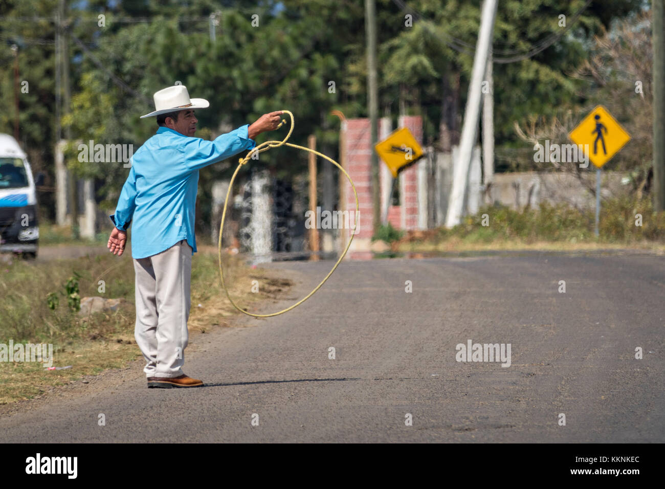 A Mexican cowboy walks down a rural road practicing his lasso skills ...