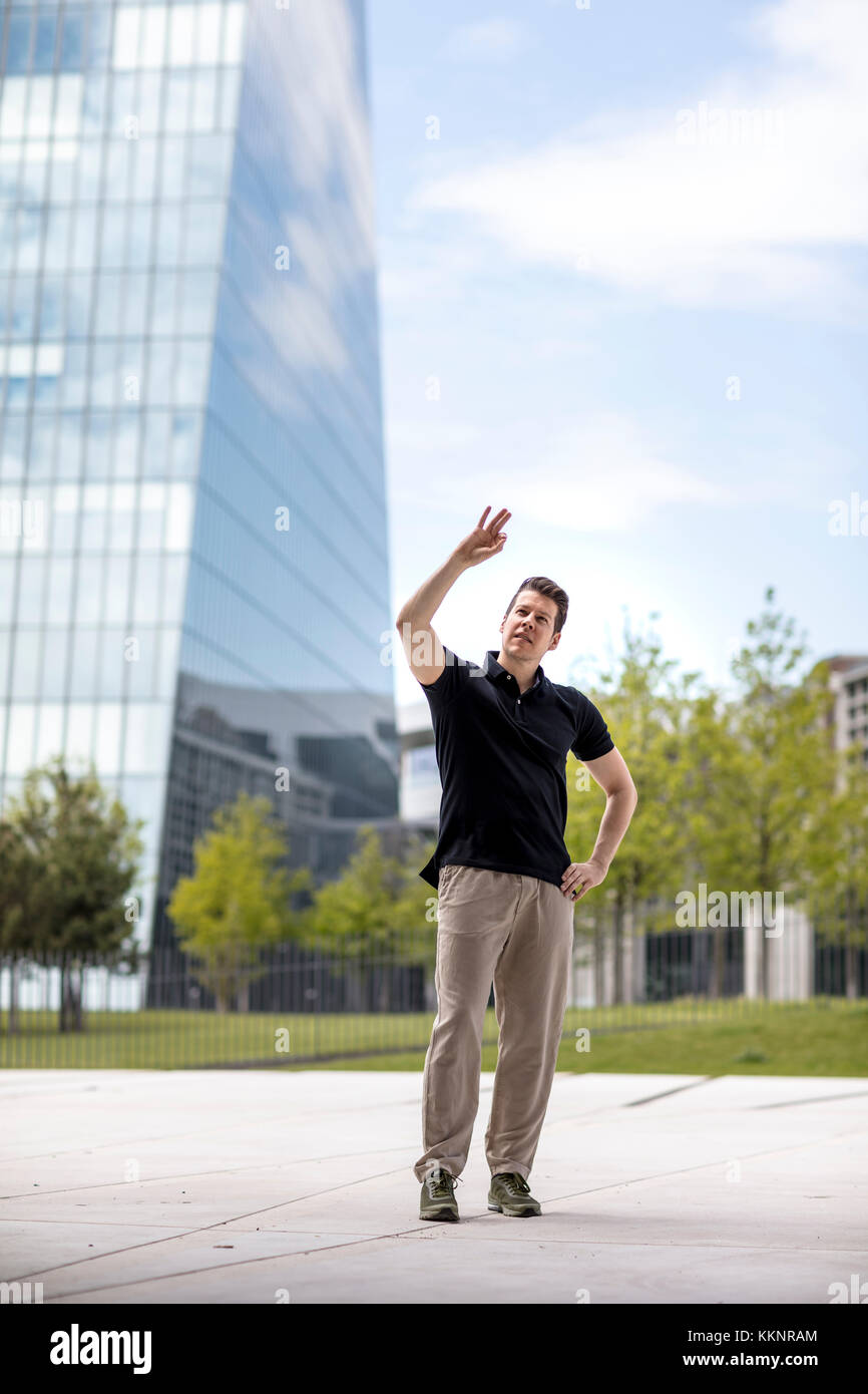 A man making hand gestures while standing in front of modern glass ...