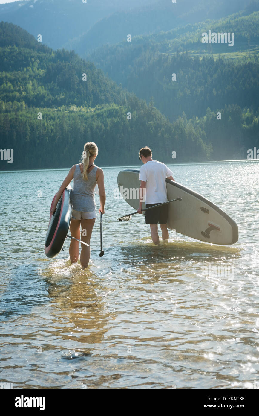 Couple with stand up paddleboard walking in river Stock Photo - Alamy