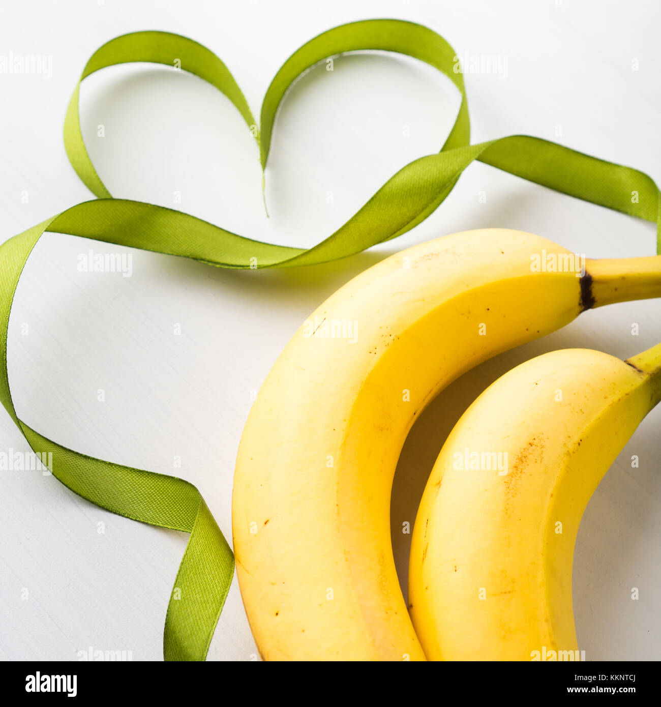 Two bananas with green ribbon frame and heart symbol on white ...