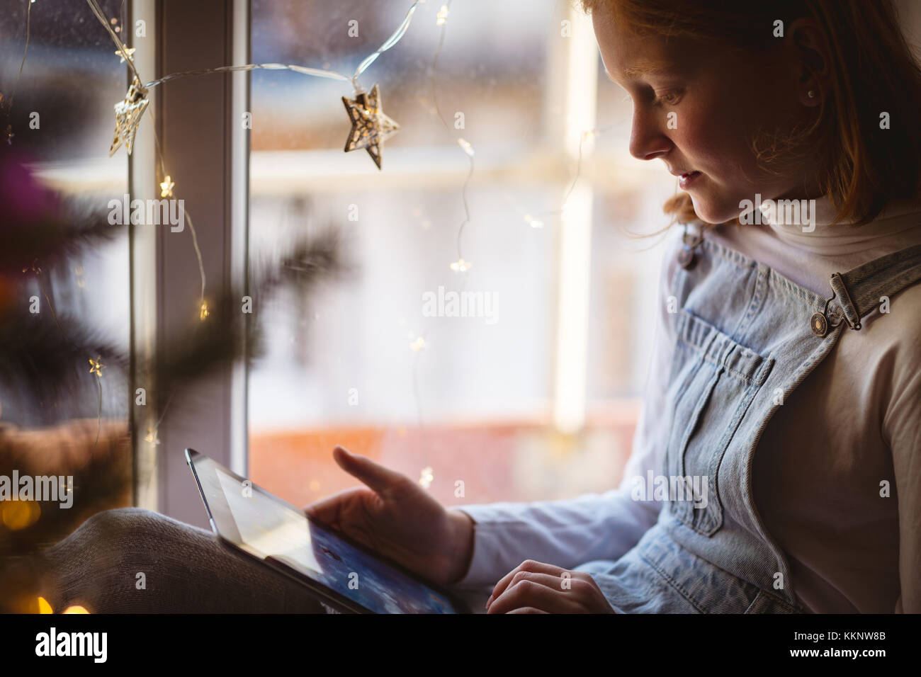 Girl sitting near window and using digital tablet at home Stock Photo ...